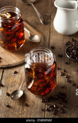 Glass with cold brew and coffee beans on yellow background, closeup ...