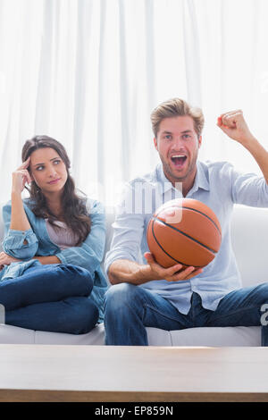 Young blonde woman holding basketball ball cheering tv game doing ok ...