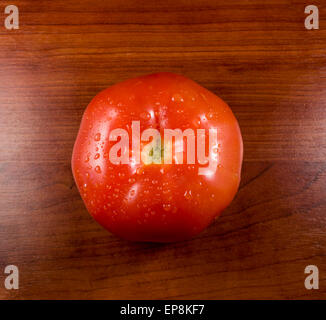 Single red ripe tomato sprayed with water with stem attached on a white ...