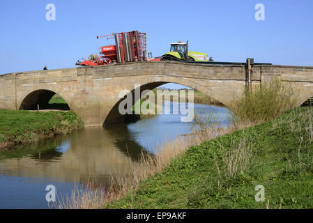 Tractor with trailer crossing over old stone bridge with water creek ...