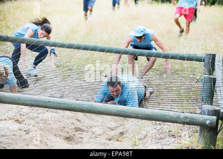 Fit woman crawling under the net during obstacle course in boot camp ...