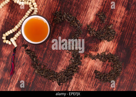 Cup of tea, dry tea leaves forming ohm symbol and buddhist necklace ...