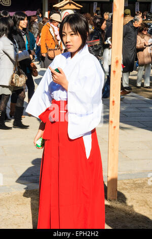 A shrine maiden in red and white robes in a courtyard at the ...