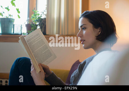 Focused adult woman reading book on couch at home, stay at home concept ...