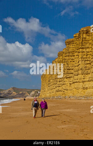 Walkers on the beach below the distinctive banded sandstone strata of ...
