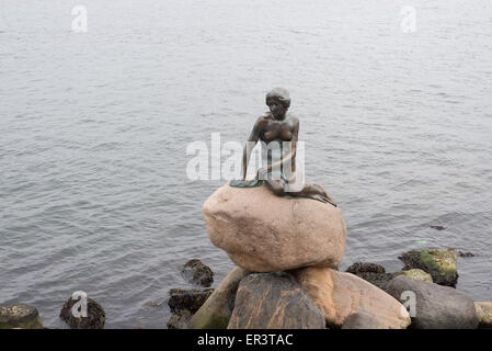 Statue of little mermaid sitting on stone. Behind it is the sea and the ...