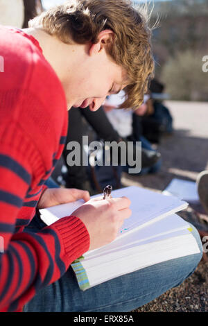 Teenage boy writing with pen in his notebook in school classroom at ...