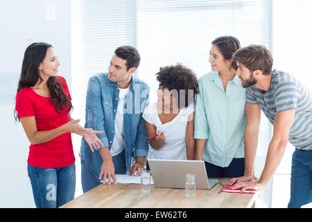Business people gathered around laptop at table in office building ...
