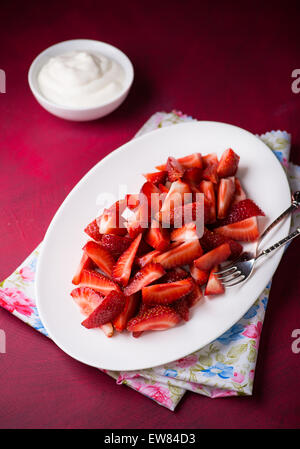 Strawberries on plate with cream over red background, selective focus ...