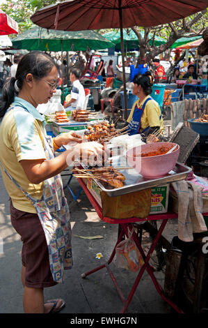 A Thai lady cooking grilled satay sticks in a Bangkok street market ...