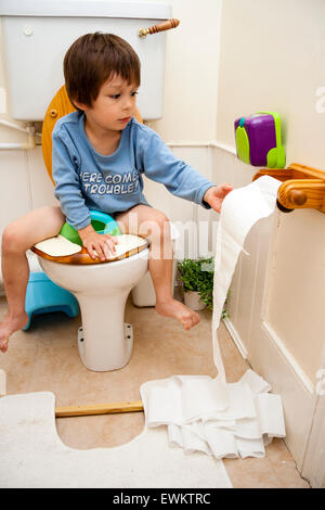 School kid sitting on toilet bowl and playing with toilet paper rolls ...