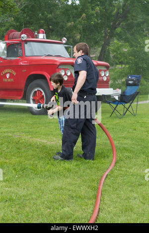 A young boy holding a fire hose putting out a fire with water spraying ...