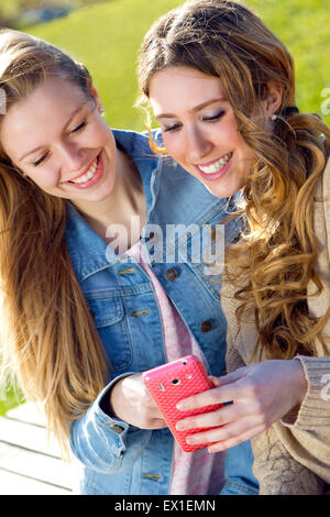 smiling friends with smartphones sitting in park Stock Photo - Alamy