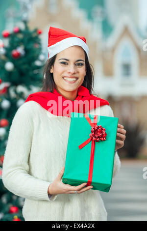 Pretty young woman with Christmas gift box sitting on sofa at home ...