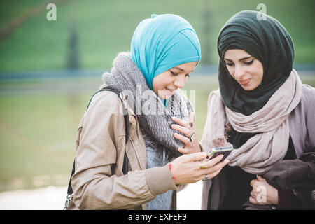 Best friends texting on smartphone while standing on sidewalk trying to ...