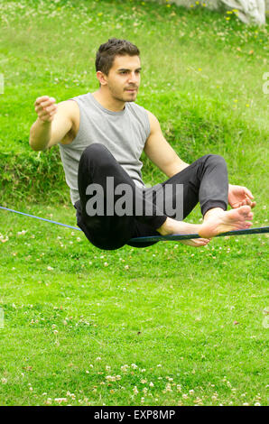 Man sitting on tightrope or slackline concentrating to keep balance ...
