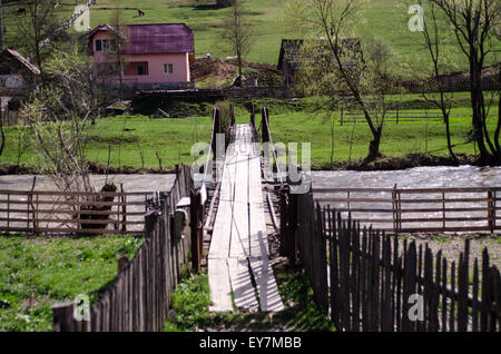 Footbridge connecting a rural village to green fields and a river under ...