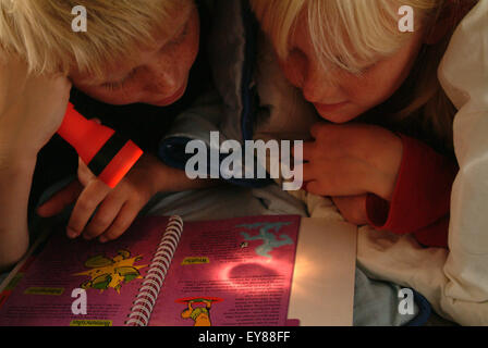 Two children snuggled up in sleeping bags reading by torchlight Stock ...