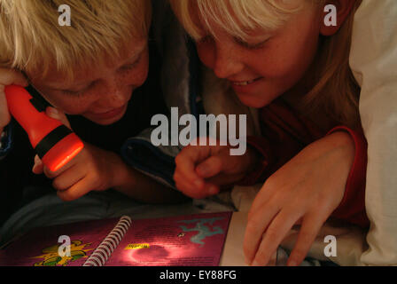Two children snuggled up in sleeping bags reading by torchlight Stock ...