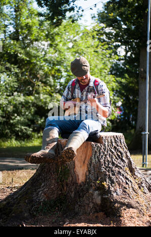 Miniature people sit on a guitar neck. Green lawn deep below them Stock ...