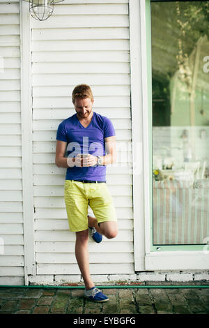 Ginger young man using mobile phone while leaning on wall indoors Stock ...