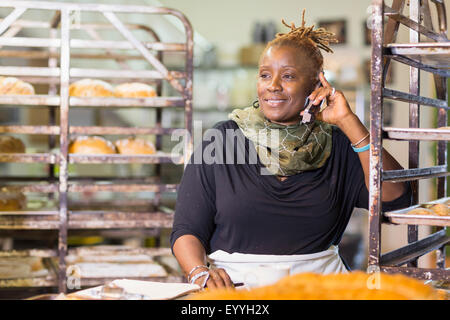 Happy woman baker talking on cell phone with laptop and bakery ...