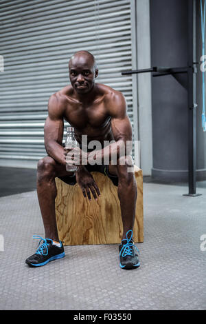 Muscular young bodybuilder sitting on chair, looking at camera ...