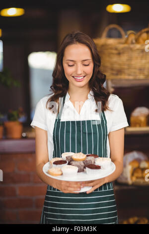 Pretty waitress showing a plate of cupcakes Stock Photo - Alamy