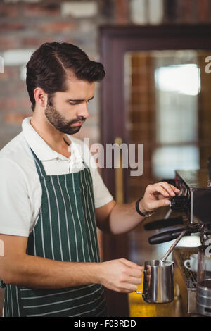 Serious bearded male barista in apron pouring ingredient from stainless ...