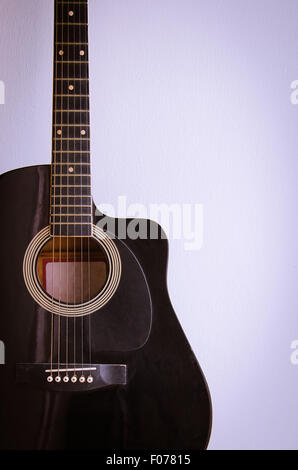 An acoustic old guitar in dust stands against a gray wall with copy ...