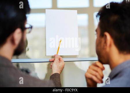 Young man pointing at blank paper sign on lilac background Stock Photo ...