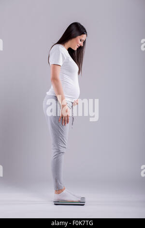 Young woman measuring her pregnant weight standing on scales ...