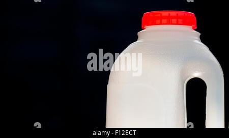 A semi-empty plastic bottle of fresh regular milk lies on a dark gray ...
