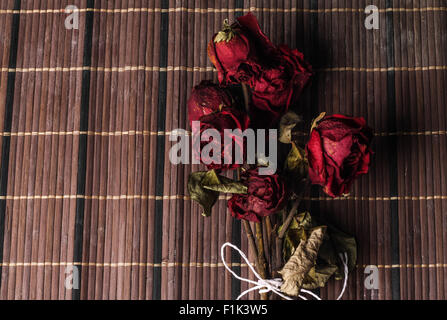 red dried rose bouquet being tied with rope. Isolated on white wooden ...