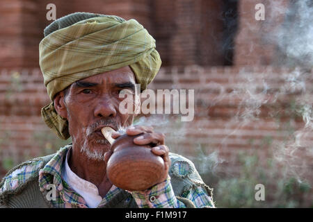 Local Burmese man smoking cigar by fire in his home in Bagan Myanmar ...