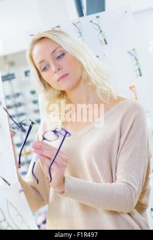 Woman comparing two pairs of eyesight glasses in front of a vision test ...