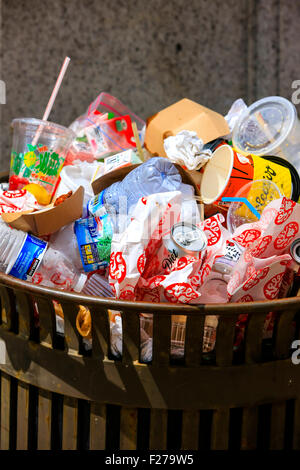 A trash can overflowing with empty drinks containers and food wrappers ...