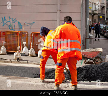 Road repair details. A worker with a manual paver aligns the hot ...