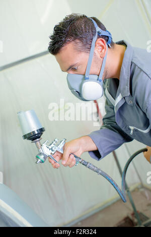 Car paint worker spraying blue paint to car body element using spray ...