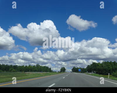 Looking down a paved highway towards fluffy, white clouds against a ...