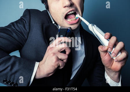 A stressed businessman is late and is shaving and brushing his teeth at ...