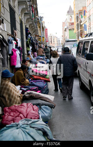 A woman is walking past used clothing and fabric remnants piled on a ...