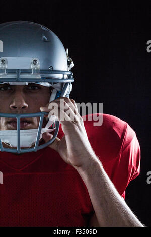 Portrait of football player holding helmet while standing on field ...