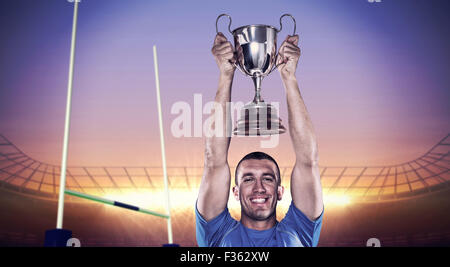 Composite image of portrait of smiling rugby player holding trophy ...