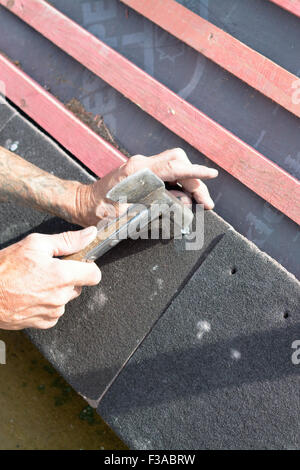 A roofer using hammer to nail tiles to wooden roof battens in Bedford ...