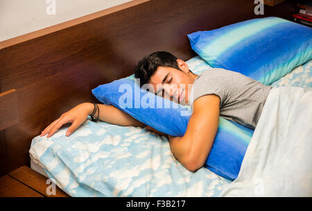 Handsome young man sleeping on blue pillow, over blankets and sheets ...