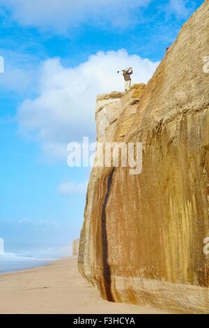 Low angle view of golder on cliff top overlooking beach taking golf ...