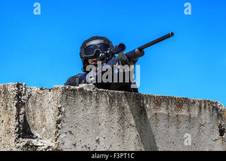Law enforcement SWAT sniper in a ghillie suit crouched in dense foliage ...