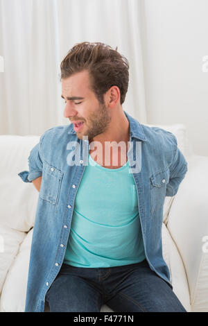 Young man suffering from back pain on sofa at home Stock Photo - Alamy