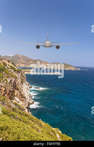 A passenger plane flying over a sea on a cloudy day with rocks and ...